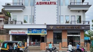 Um hotel chamado Aishwarya com fachada moderna, várias varandas e uma placa de agência de viagens abaixo.