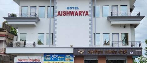 Um hotel chamado Aishwarya com fachada moderna, várias varandas e uma placa de agência de viagens abaixo.