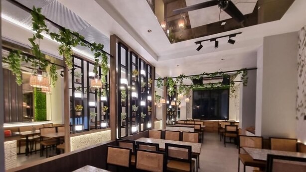 Um restaurante com mesas dentro, plantas penduradas e um design de teto moderno.