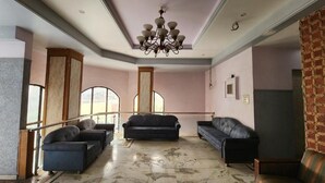 Uma sala de estar ampla com piso de mármore, vários sofás, um candelabro e grandes janelas.