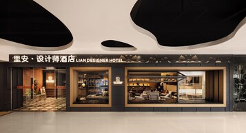 Um hotel com design moderno, apresentando uma área de recepção com fachada de vidro, espaço de estar com mesas e cadeiras, e uma placa com o nome do hotel.