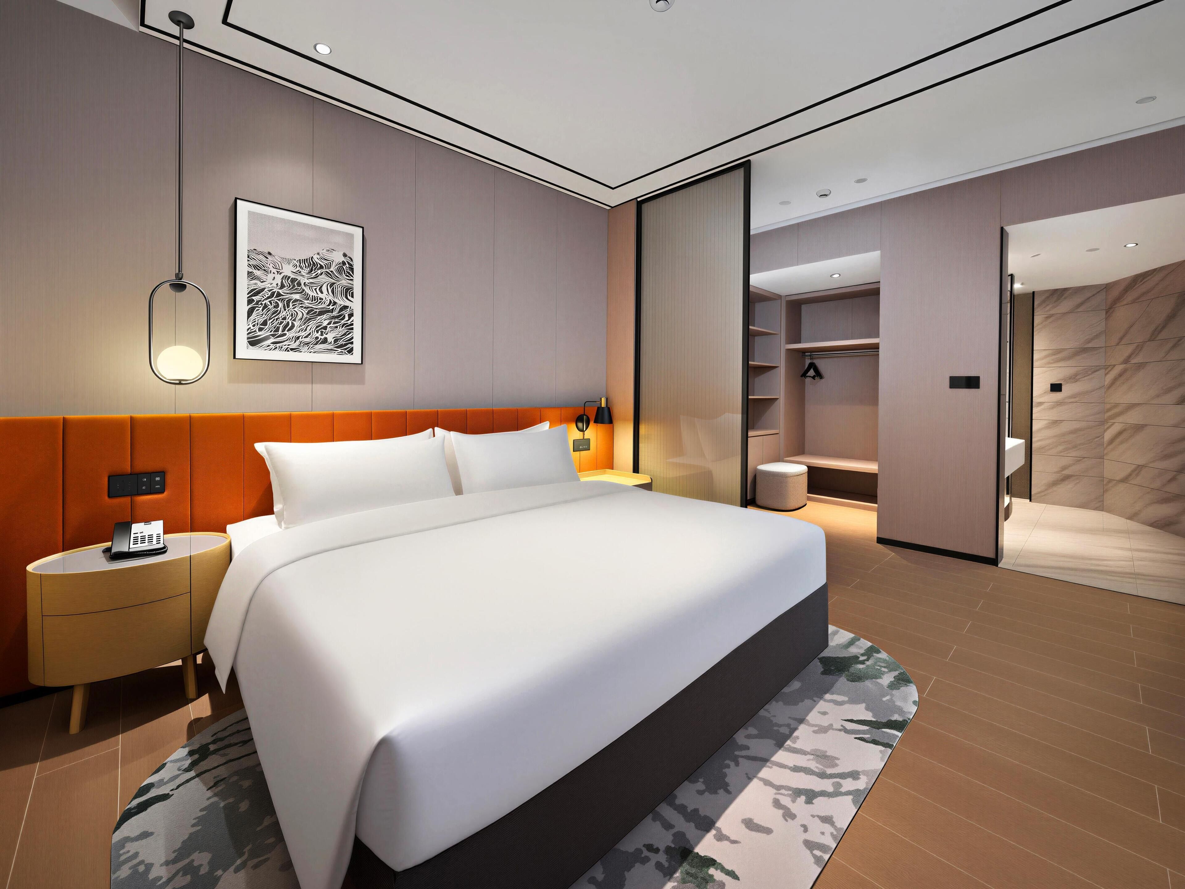 Quarto de hotel moderno com cama grande, mesa de cabeceira e guarda-roupa.