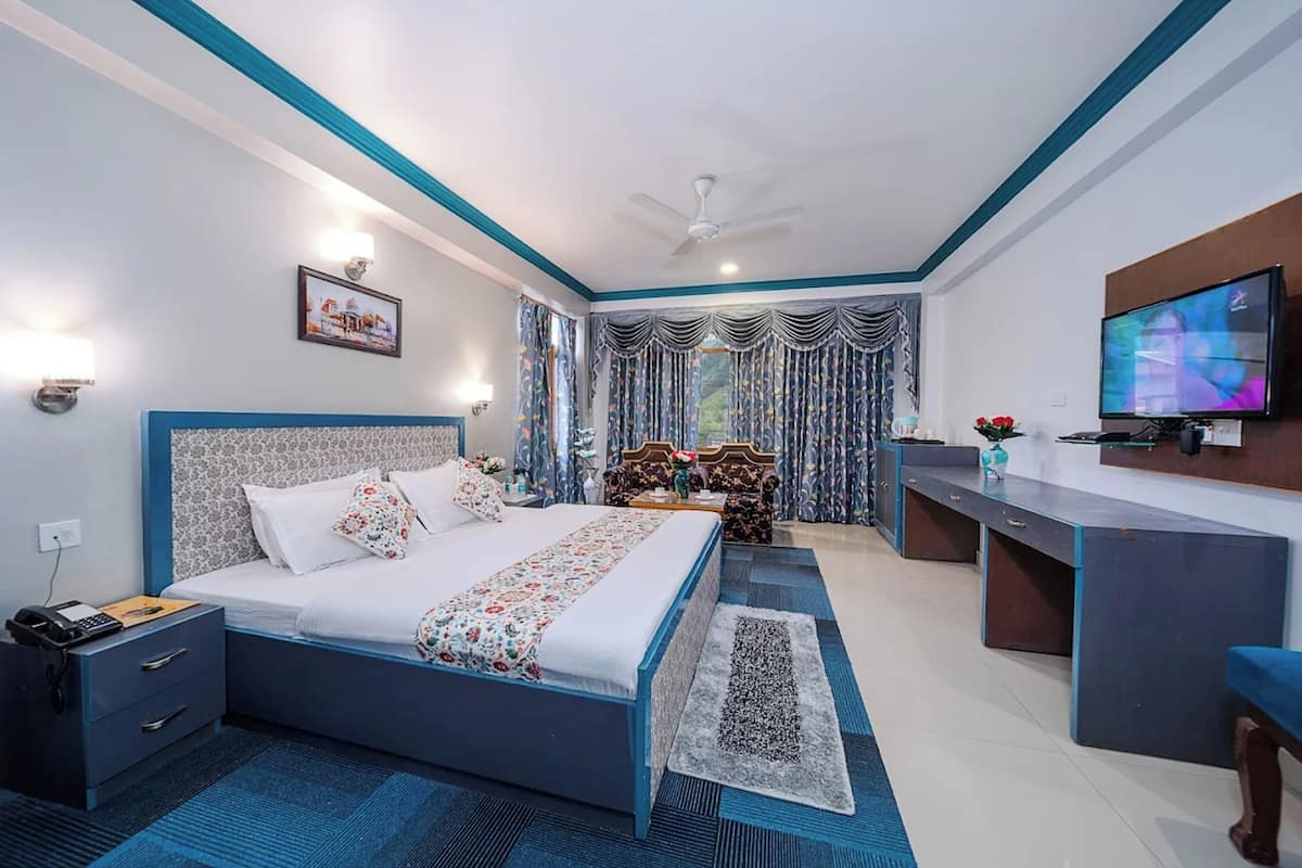 Quarto de hotel com cama, escrivaninha, televisão e cortinas.