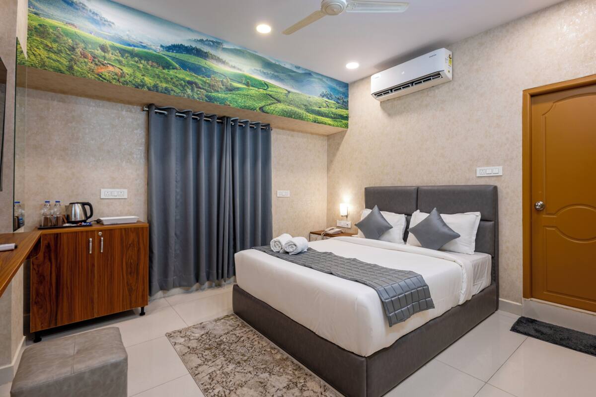 Quarto com cama, mesa de cabeceira, escrivaninha com chaleira e guarda-roupa.