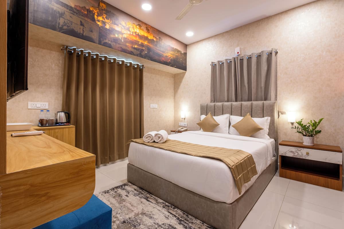 Quarto de hotel com cama, escrivaninha, mesa de cabeceira, televisão e um quadro na parede.