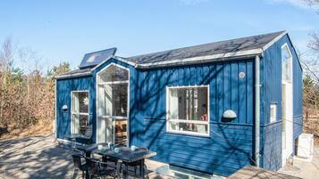 Uma casa de madeira azul com um alpendre, uma mesa e cadeiras.