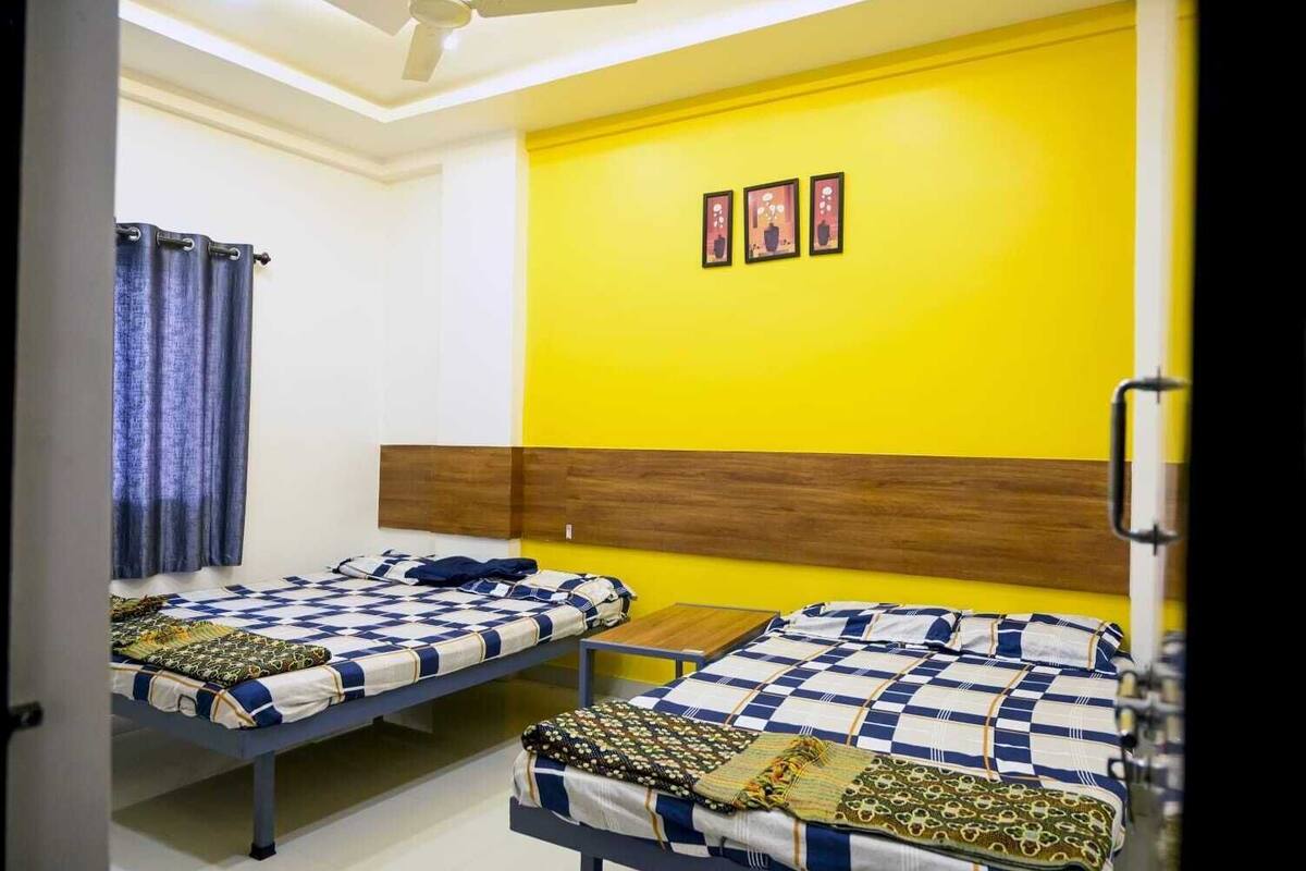 Quarto com duas camas, ventilador de teto e parede amarela.
