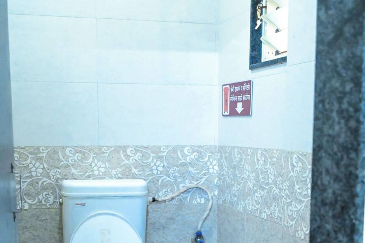 Um banheiro com vaso sanitário, um balde azul e uma torneira fixada na parede.