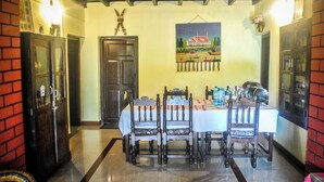 Uma área de jantar com uma mesa posta para quatro pessoas, rodeada por cadeiras de madeira, um quadro na parede e uma porta com um objeto decorativo acima.