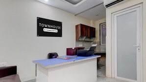 Uma mesa de recepção com uma placa indicando 'TOWNHOUSE Company-Serviced', um balcão, uma cadeira, uma impressora e uma porta.