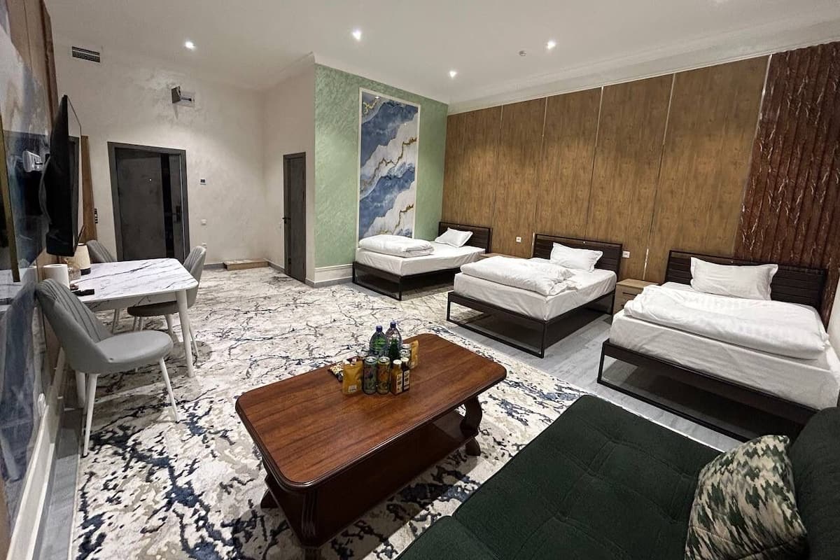Quarto de hotel com área de refeições, duas camas, um sofá, uma mesa de centro com bebidas e uma grande pintura abstrata na parede.