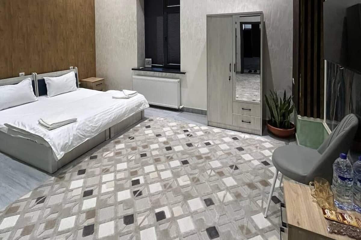Quarto de hotel com cama, escrivaninha, cadeira, guarda-roupa e televisão.