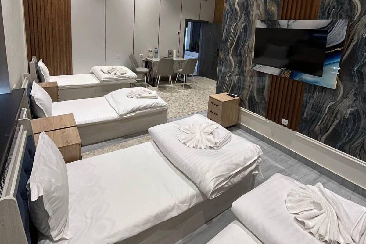 Quarto de hotel com um espelho grande, televisão de tela plana, escrivaninha e três camas.
