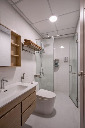 Casa de banho moderna com lavatório branco, toucador de madeira e zona de duche com vedação de vidro.