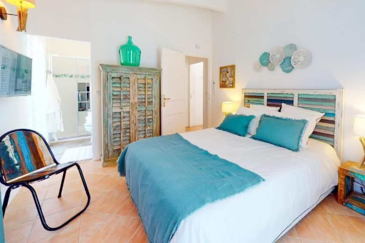 Quarto com cama, uma cadeira, um armário e uma mesinha de cabeceira com abajur.