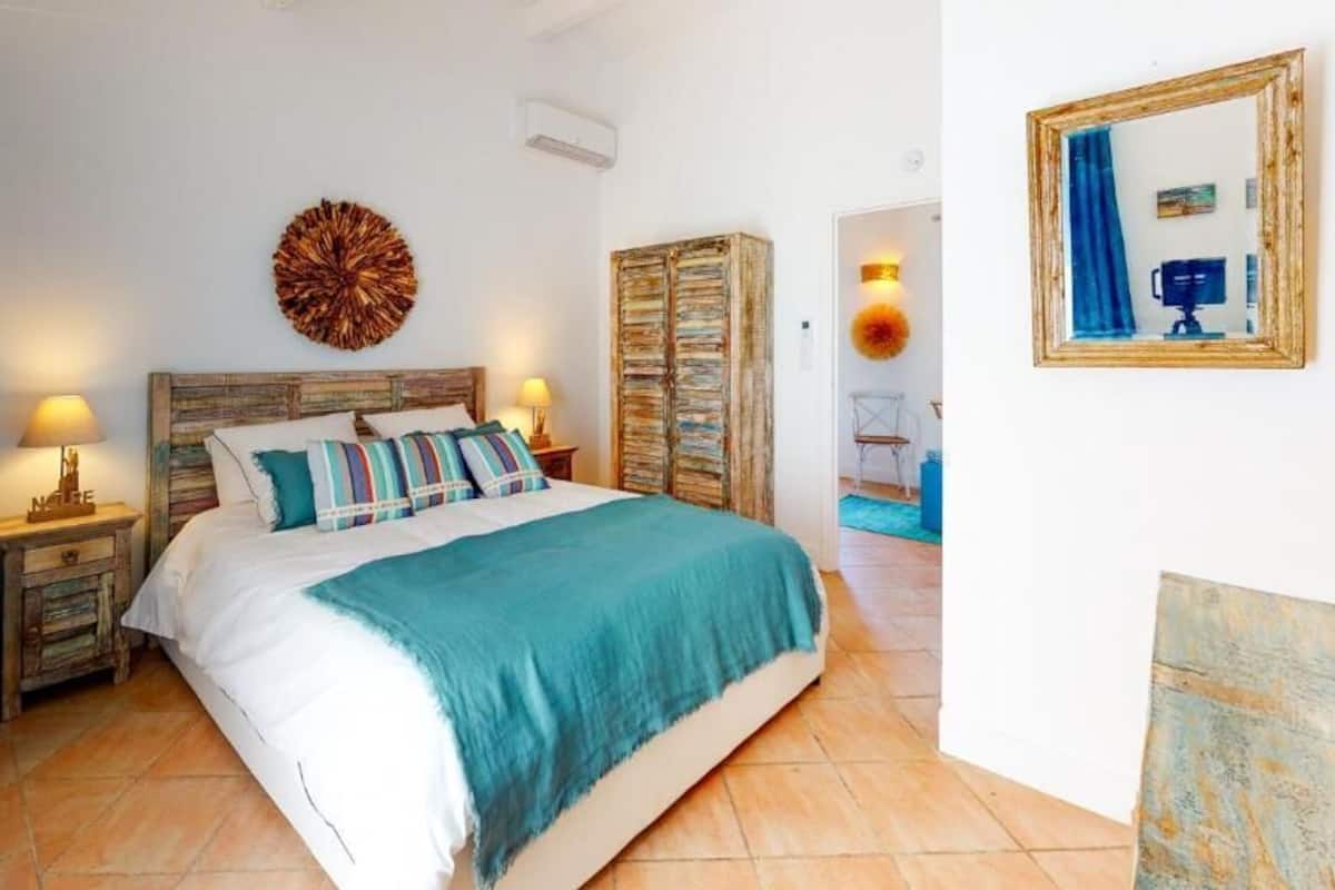 Quarto com cama, mesa de cabeceira, espelho na parede e porta.