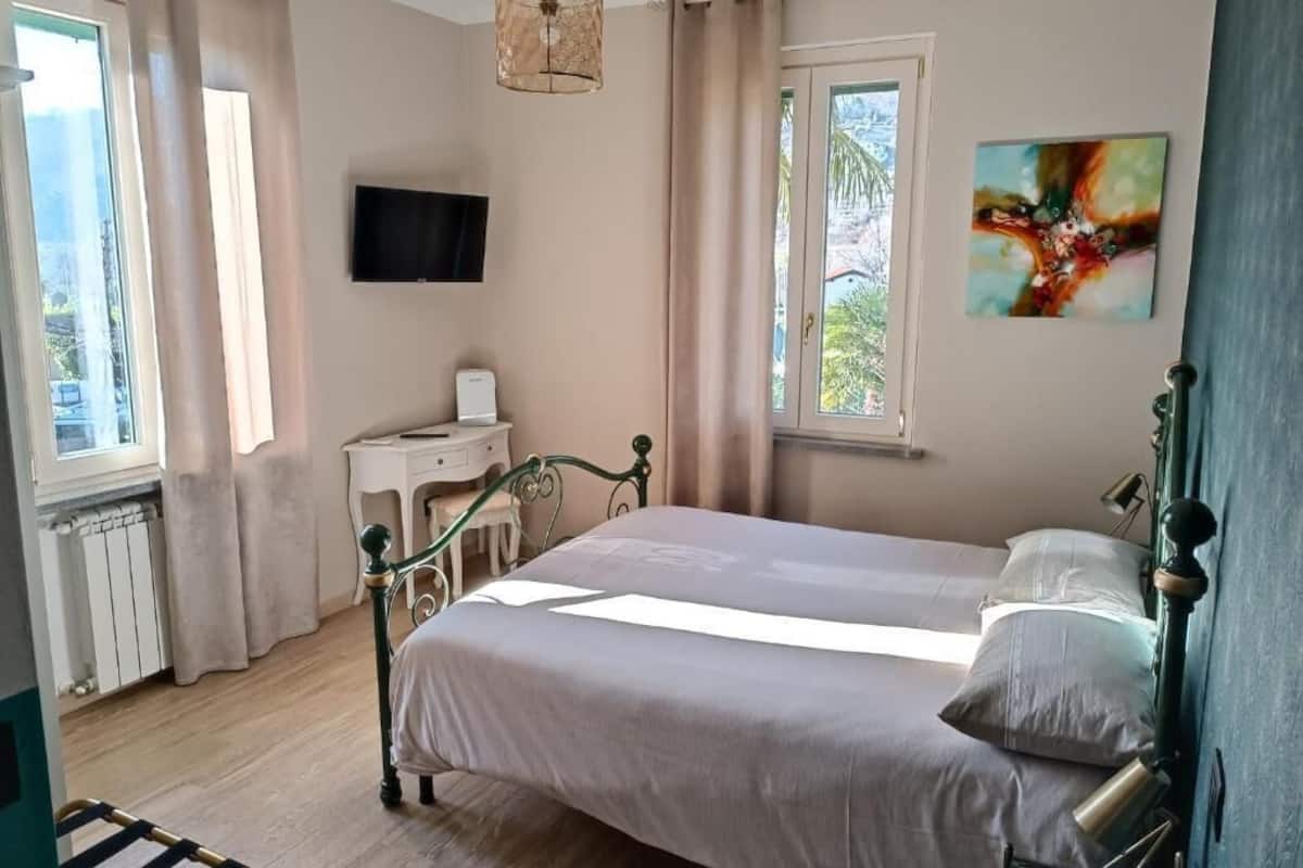 Quarto com cama, escrivaninha, televisão e janela com cortinas.
