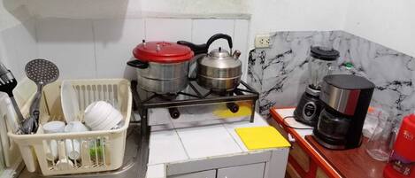 Uma cozinha com pia, fogão, chaleira, cafeteira e escorredor de louça.