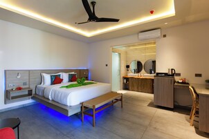 Quarto de hotel moderno com cama, mesa de cabeceira, banco, escrivaninha, cadeira e ventoinha.