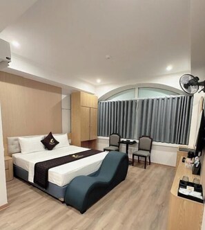 Quarto de hotel com cama, escrivaninha, cadeira, janela com cortinas e ventilador de teto.