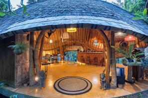 Uma estrutura com telhado de palha, área de bar, assentos e plantas decorativas.