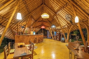 Decoração temática em bambu, com área de bar central, espaços para sentar e ventoinha no teto.