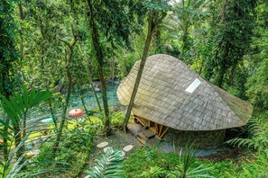 Uma cabana com telhado de palha, rodeada por vegetação exuberante e um corpo d'água límpido.