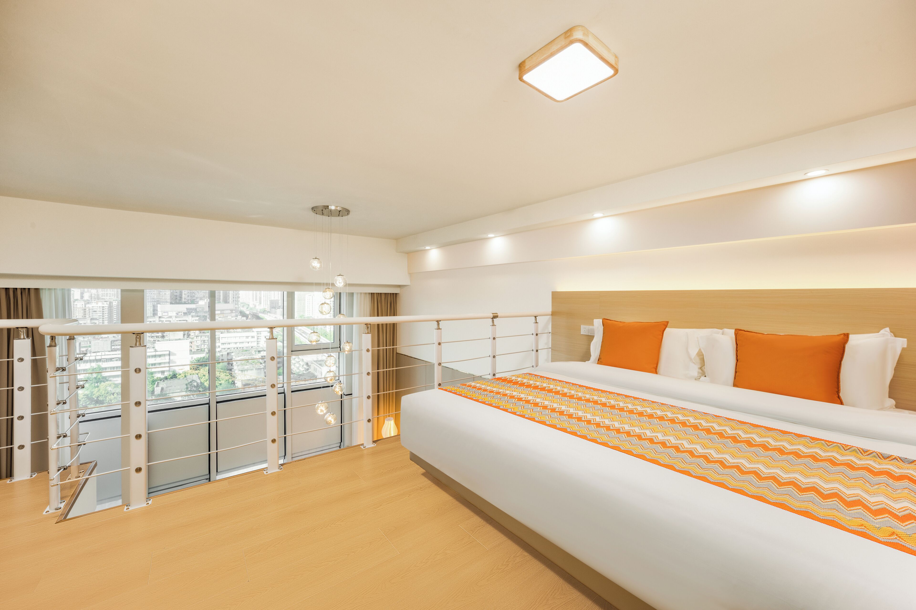 Quarto de hotel com varanda, cama com colcha laranja e branca, e vista para a paisagem urbana.