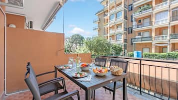 Varanda com mesa posta para refeição, cercada por grade de metal e vista para um prédio residencial.