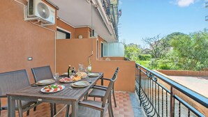 Área de refeições ao ar livre com uma mesa posta para dois, cadeiras e vista para o verde.
