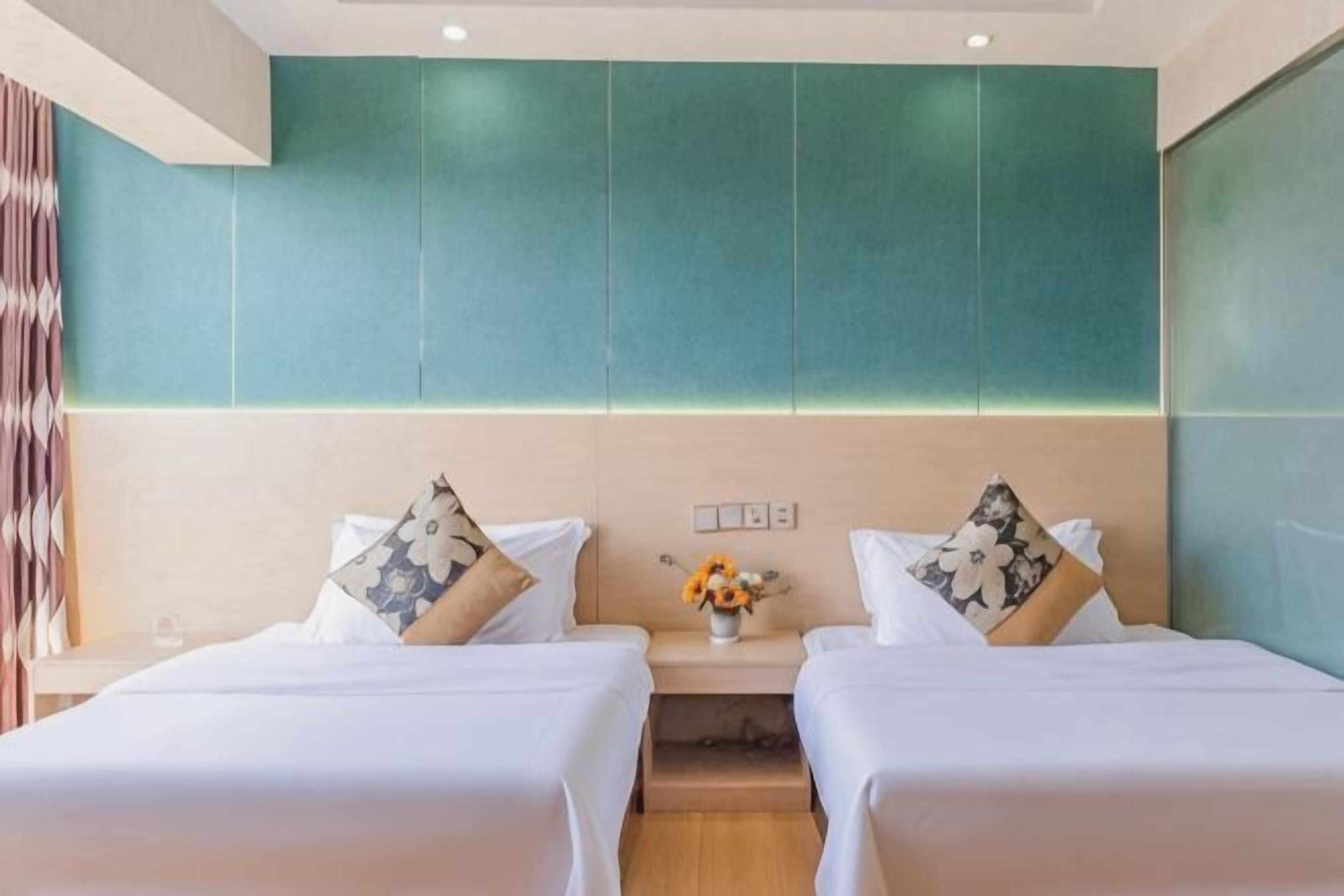 Quarto de hotel com duas camas, uma mesa de cabeceira e um vaso com flores.