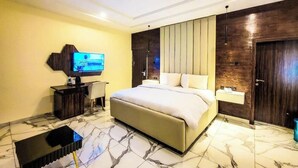 Quarto de hotel moderno com uma cama grande, televisão, pequena escrivaninha e mesa de cabeceira.