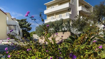 Um edifício com várias andares e varandas, rodeado por vegetação e flores.
