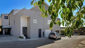 Um edifício moderno de dois andares com um carro estacionado na frente, uma porta de garagem visível e céu claro.