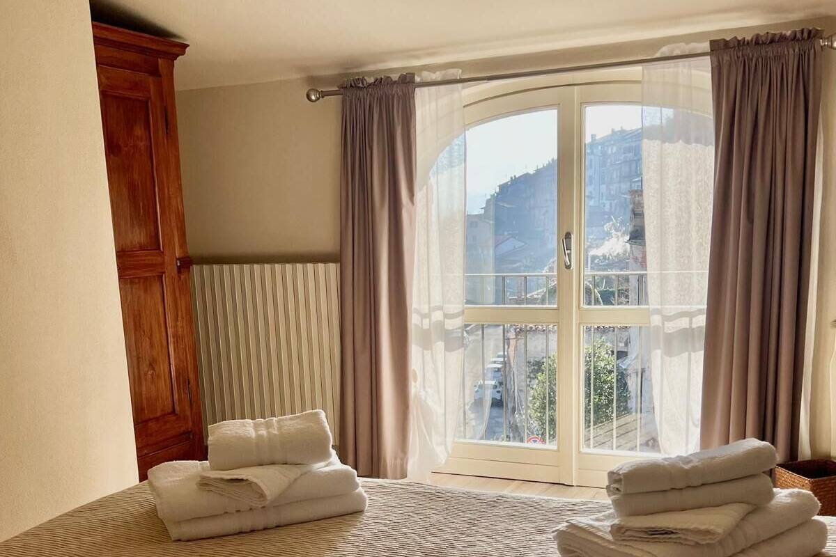 Quarto de hotel com uma cama grande, um guarda-roupa de madeira e vista através de uma porta de vidro.