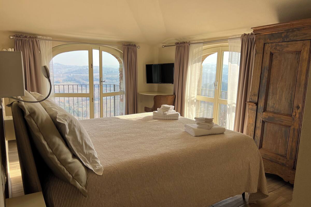 Quarto de hotel com uma cama grande, televisão, guarda-roupa de madeira e varanda com vista.