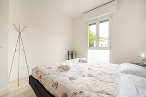 Quarto com cama, janela, luminária de chão e mesa de cabeceira.