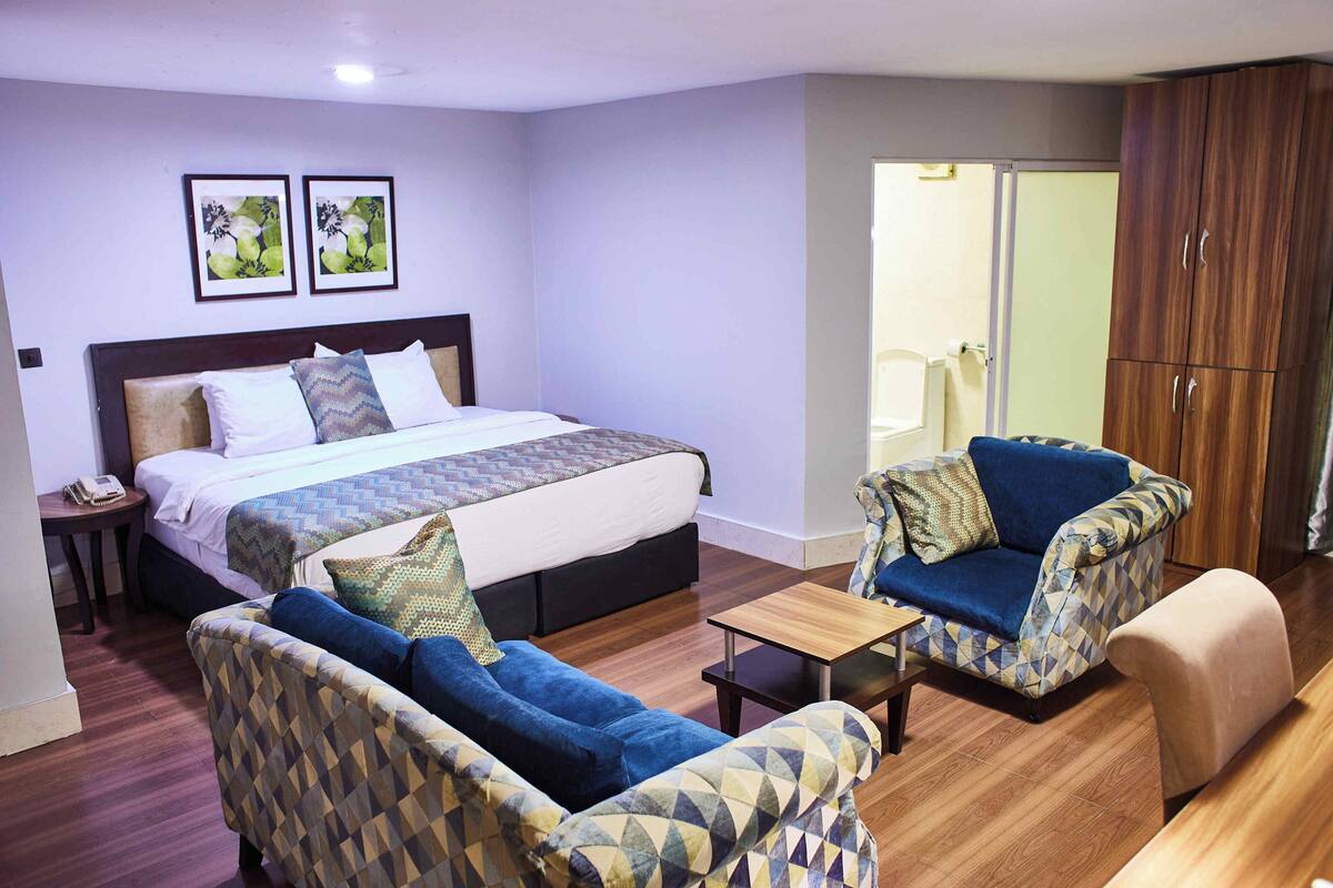 Quarto de hotel com uma cama, duas poltronas, uma pequena mesa e um guarda-roupa.