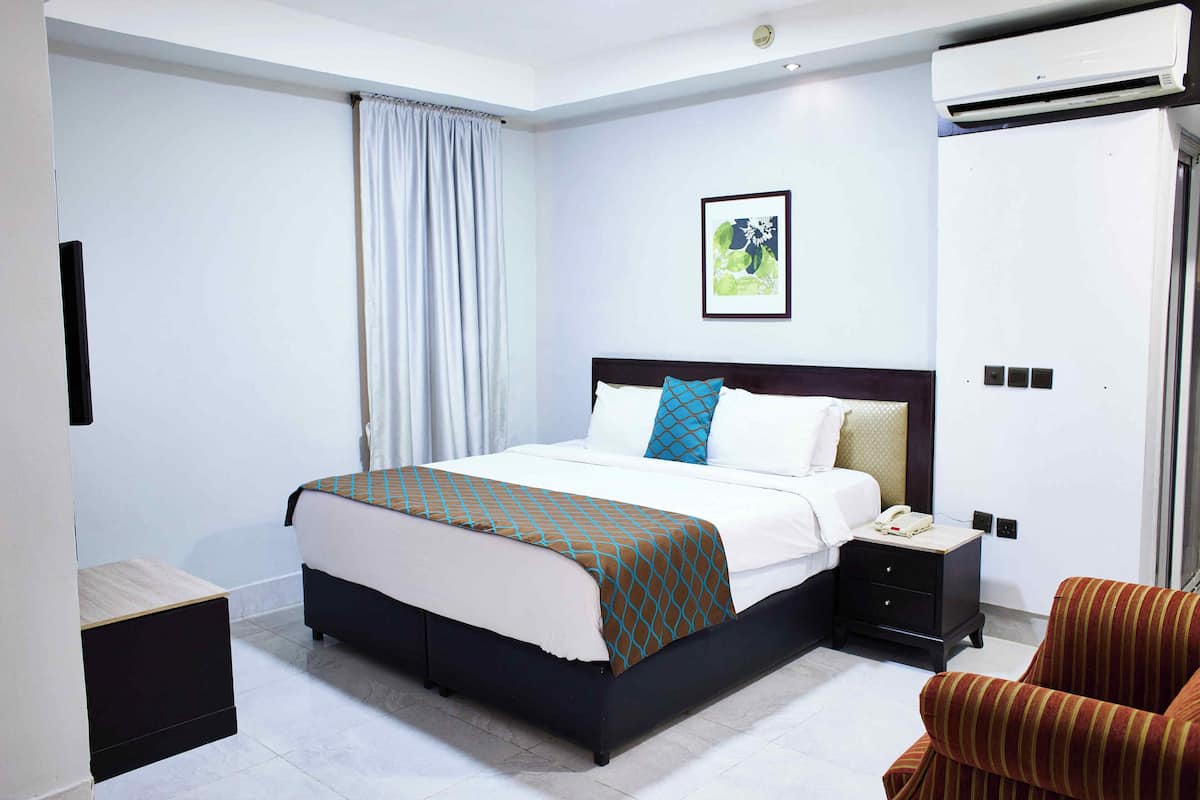 Quarto de hotel com cama, mesa de cabeceira, cadeira e aparelho de ar condicionado.