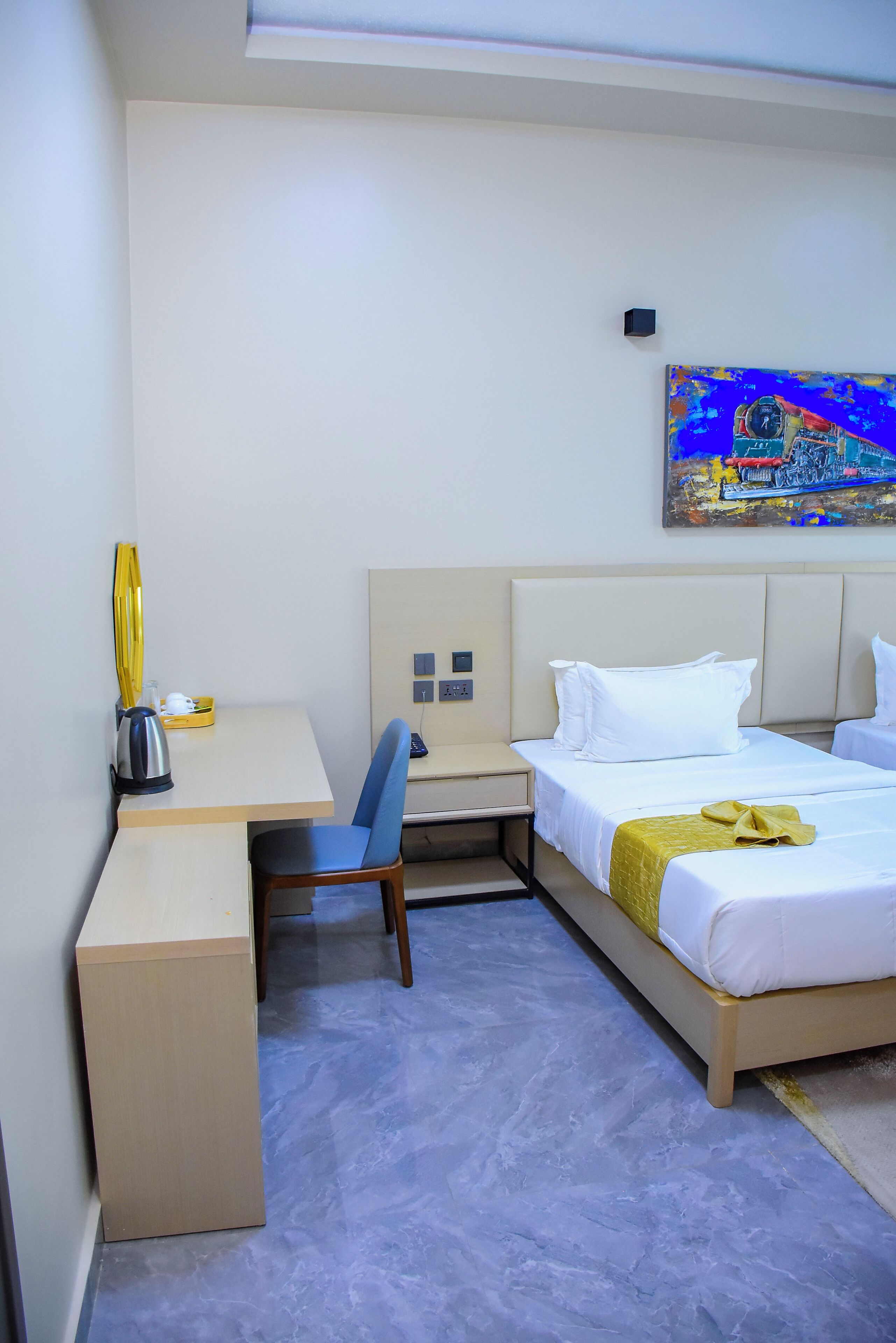 Quarto de hotel com cama, escrivaninha, cadeira, cafeteira e um quadro na parede.