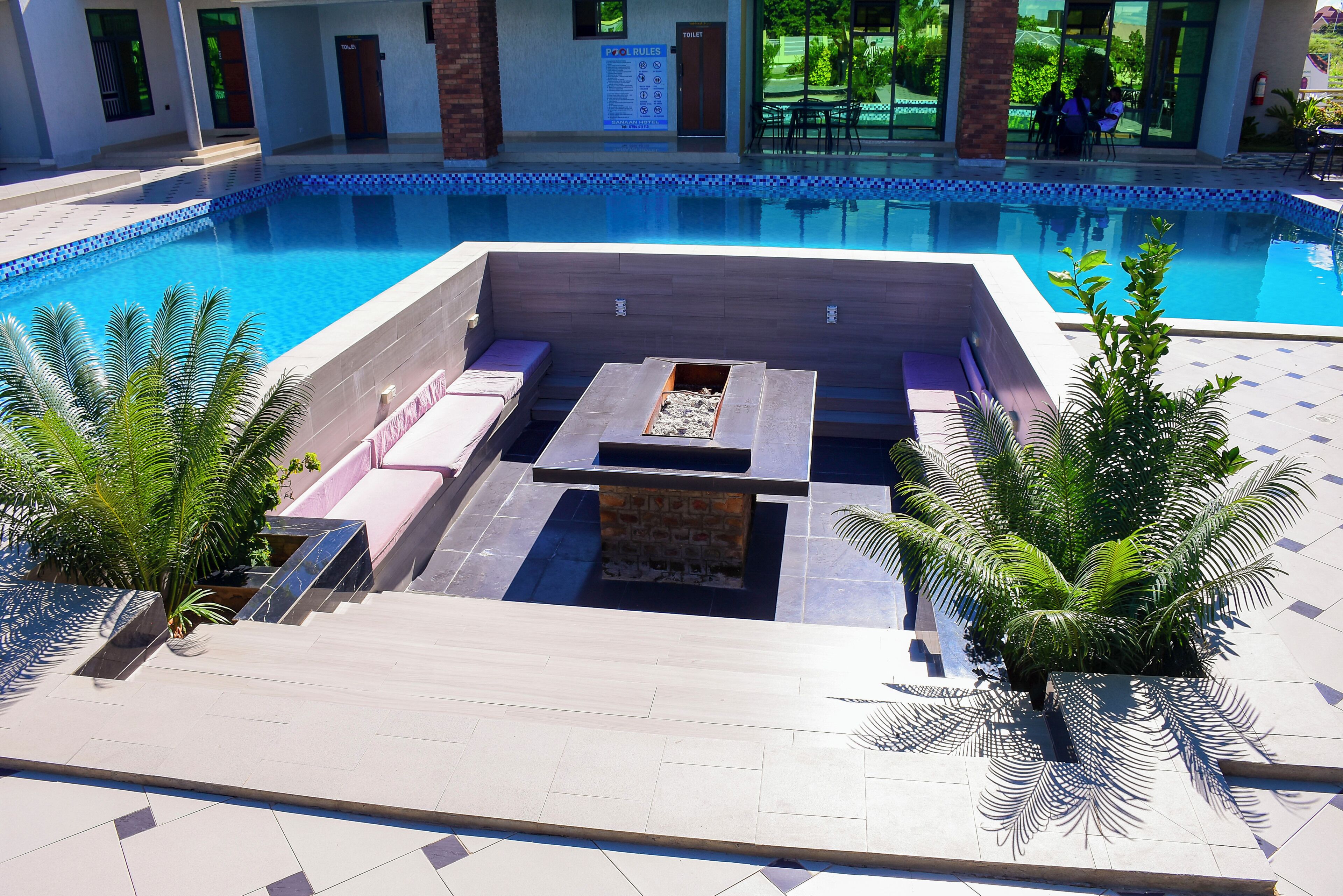 Piscina com área de espreguiçadeiras, lareira e vegetação ao redor.