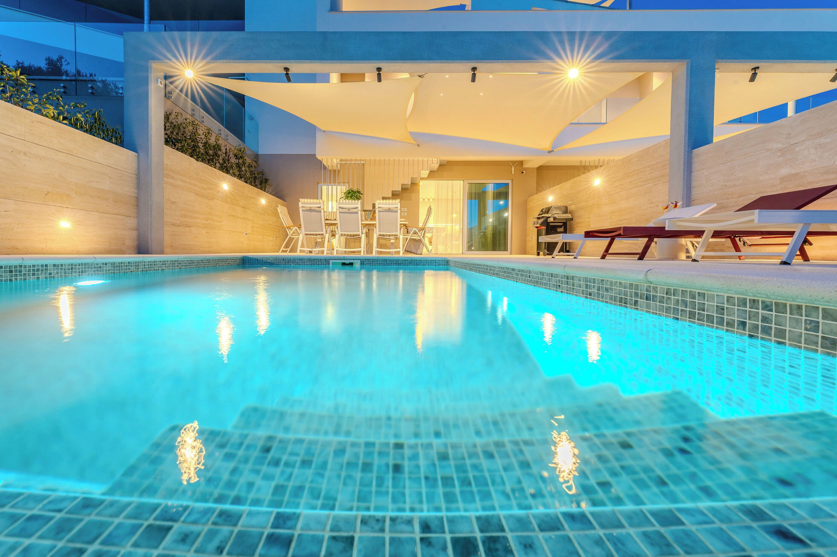 Piscina interior moderna com água azul cristalina, rodeada por espreguiçadeiras e uma escadaria que dá acesso a um andar superior.