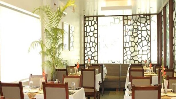 Um restaurante com mesas, cadeiras, um painel decorativo e uma planta.