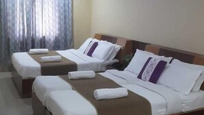 Quarto de hotel com duas camas, ventoinha no teto, ar condicionado e janela com cortinas.
