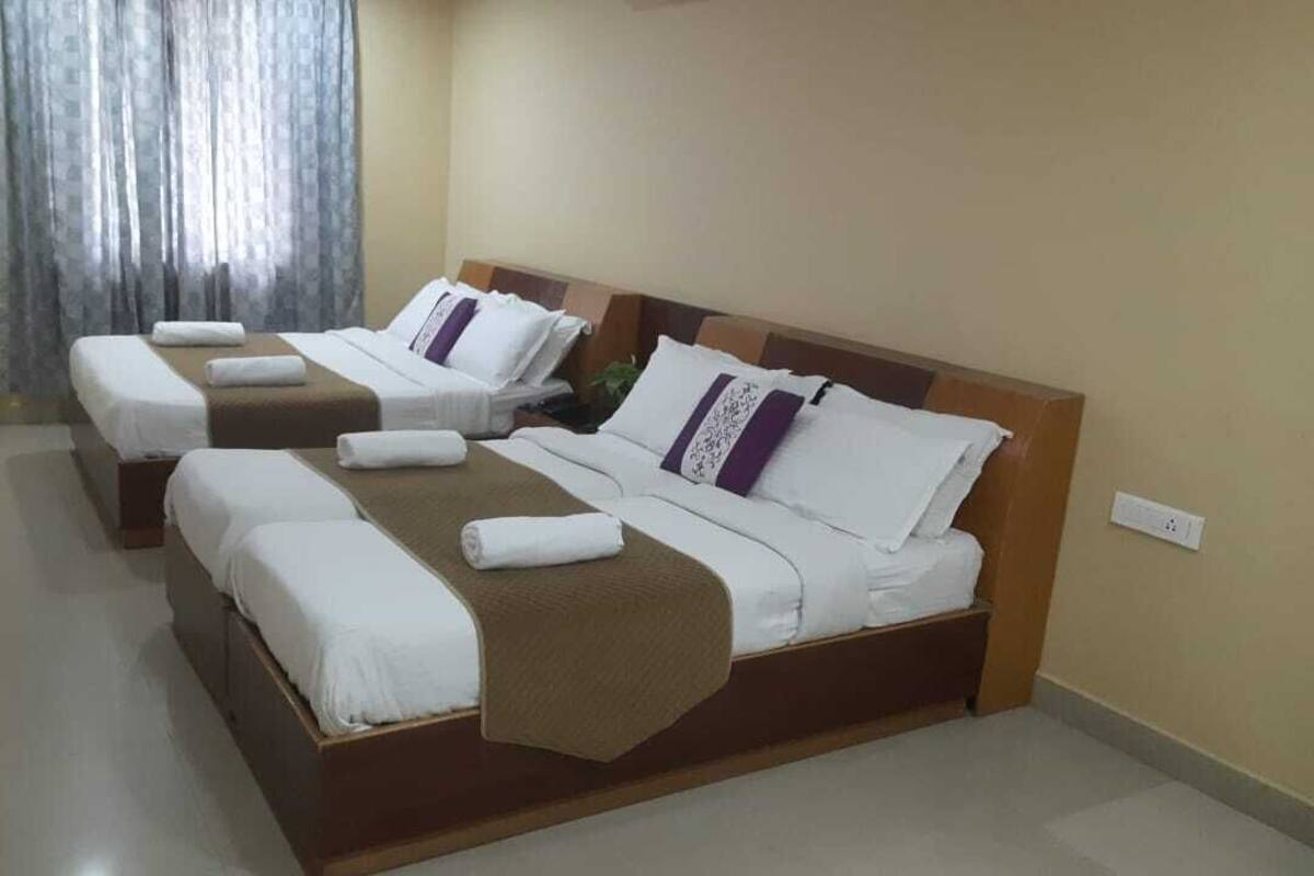 Quarto de hotel com duas camas, cabeceira de madeira e janela com cortinas.