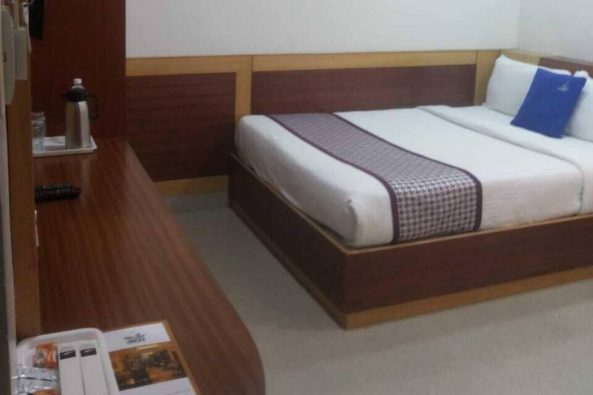 Quarto de hotel com cama, mesa de cabeceira, ventoinha no teto e um quadro na parede.