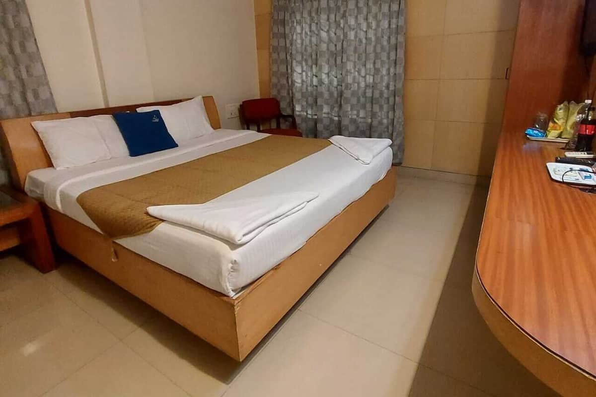 Quarto de hotel com uma cama, mesa de cabeceira de madeira, uma cadeira, televisão e cortina.