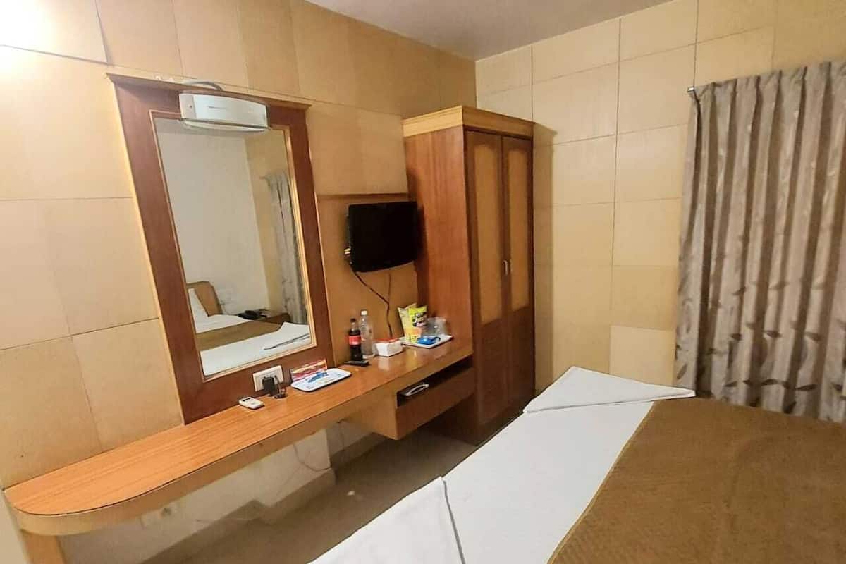 Quarto de hotel com escrivaninha de madeira, televisão, cama e cortina.