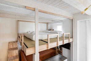 Uma cama beliche com estrutura de madeira, colchão, travesseiros e uma mesinha de cabeceira.