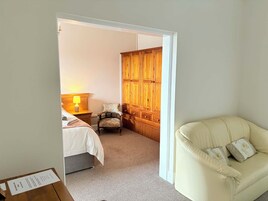 Quarto de hotel com cama, uma cadeira, um guarda-roupa de madeira e um sofá bege.